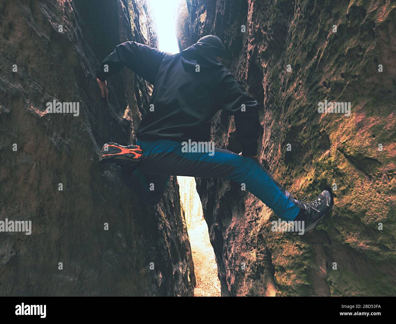 Funny man is climbing in thin distance between two rocks. Dark corner ...