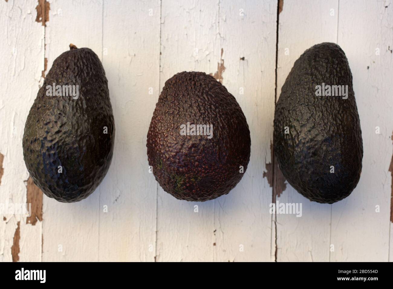 3 avocados photographed from above on a white rustic wooden background ...
