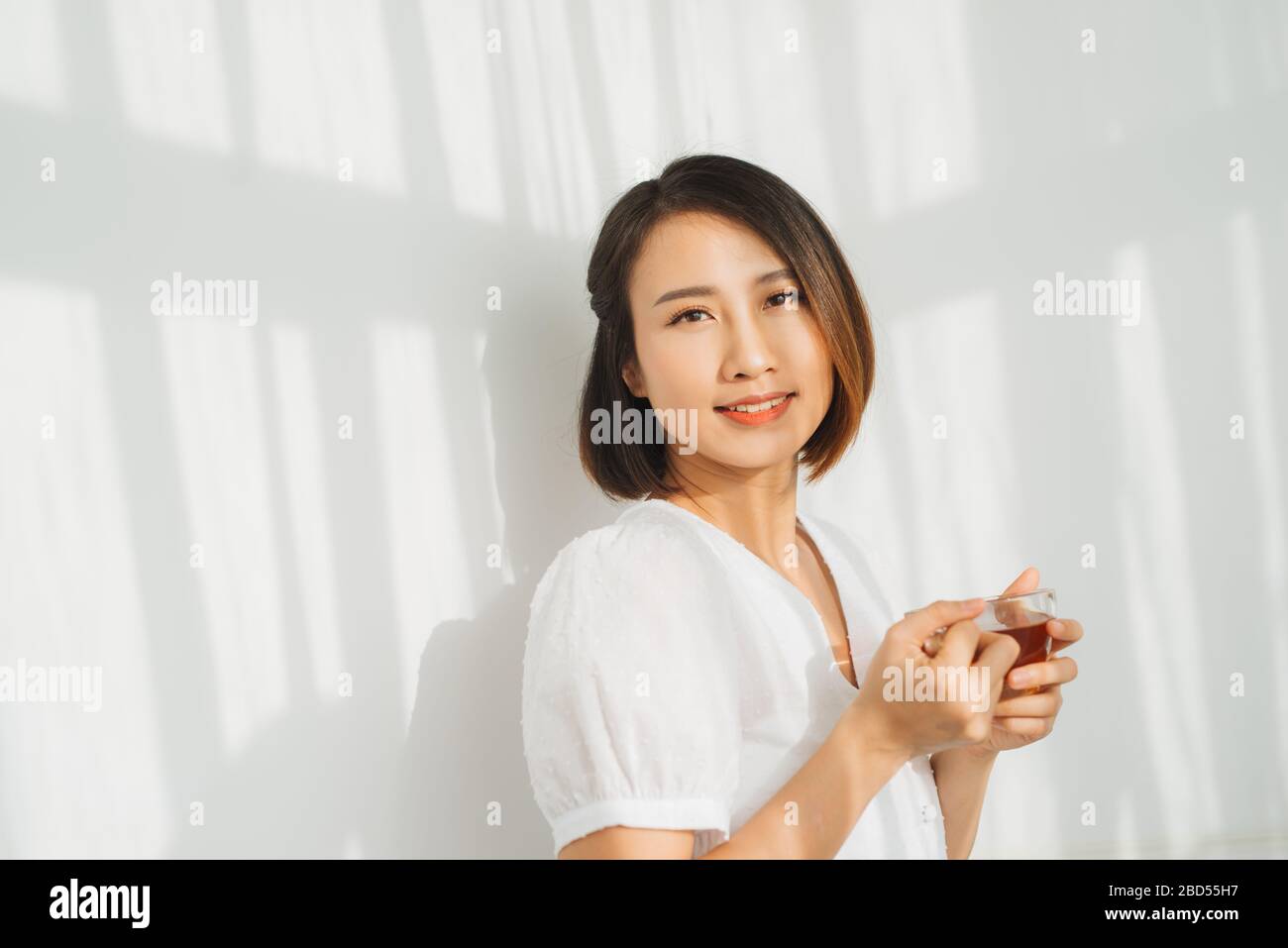 Beautiful woman standing by the window with a glass of hot tea in hand ...