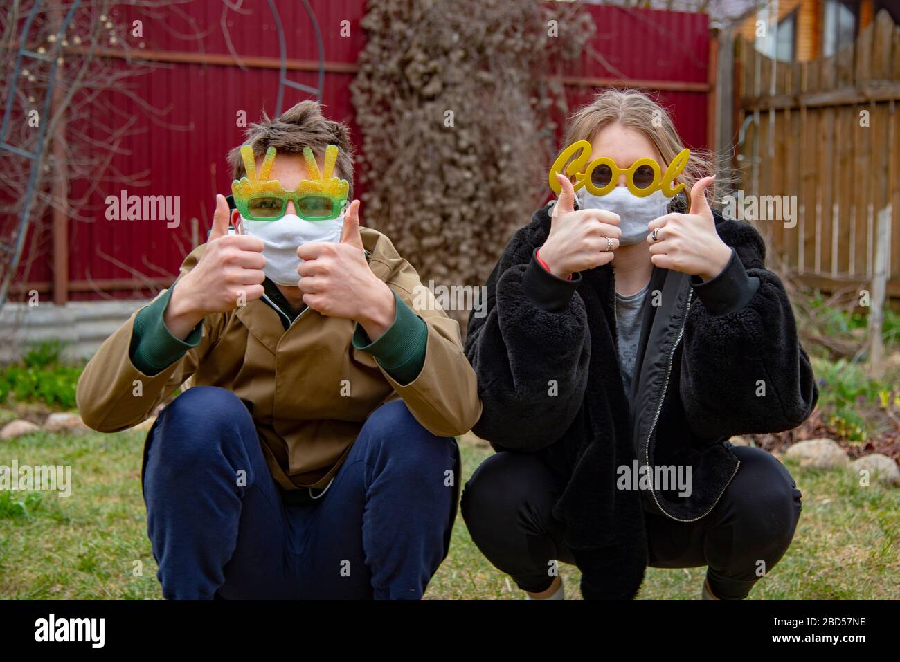 Two teenagers in protective medical masks and funny glasses make ...