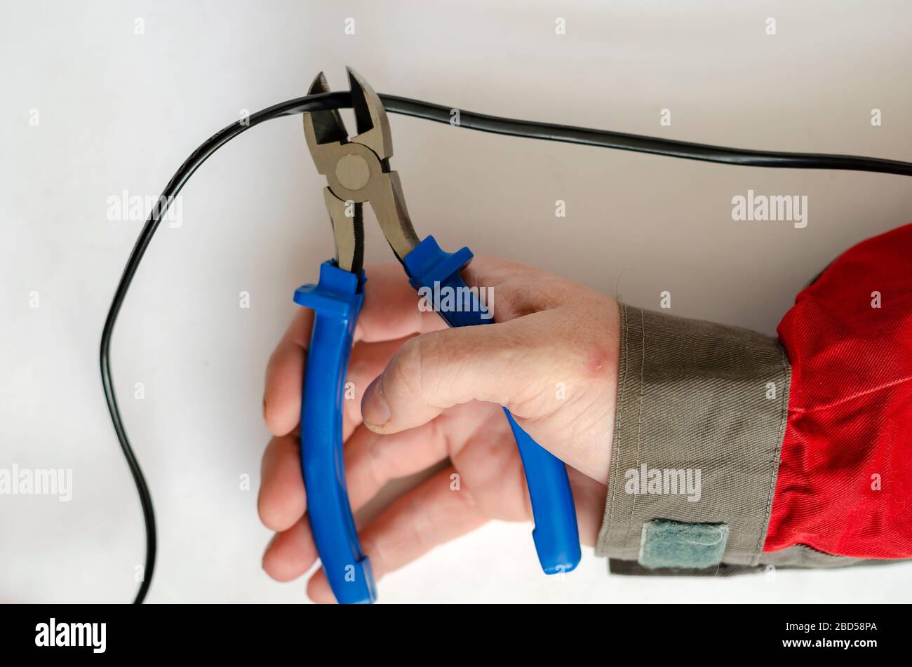 A man's hand holds a wire cutter. A man in work clothes cuts the ...