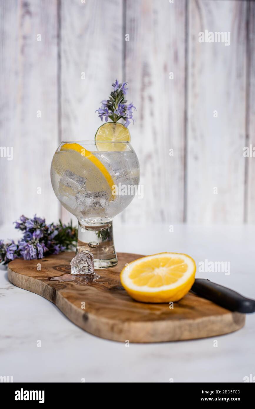 Cold Gin & Tonic cocktail with lemon garnish on wooden chopping board ...