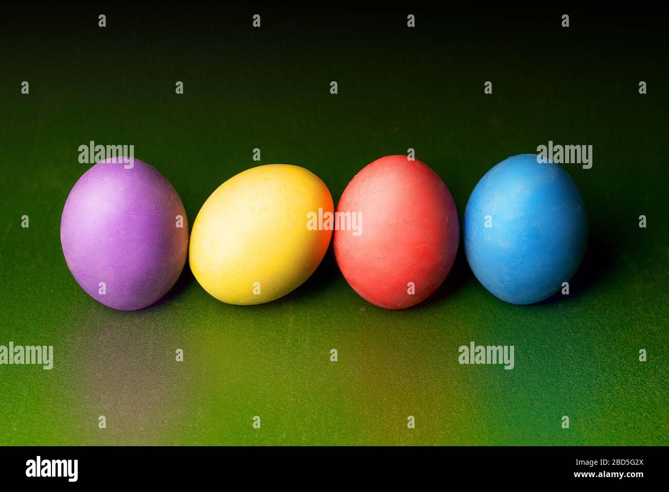 Colorful gypsum easter eggs on green background in a row with reflected ...