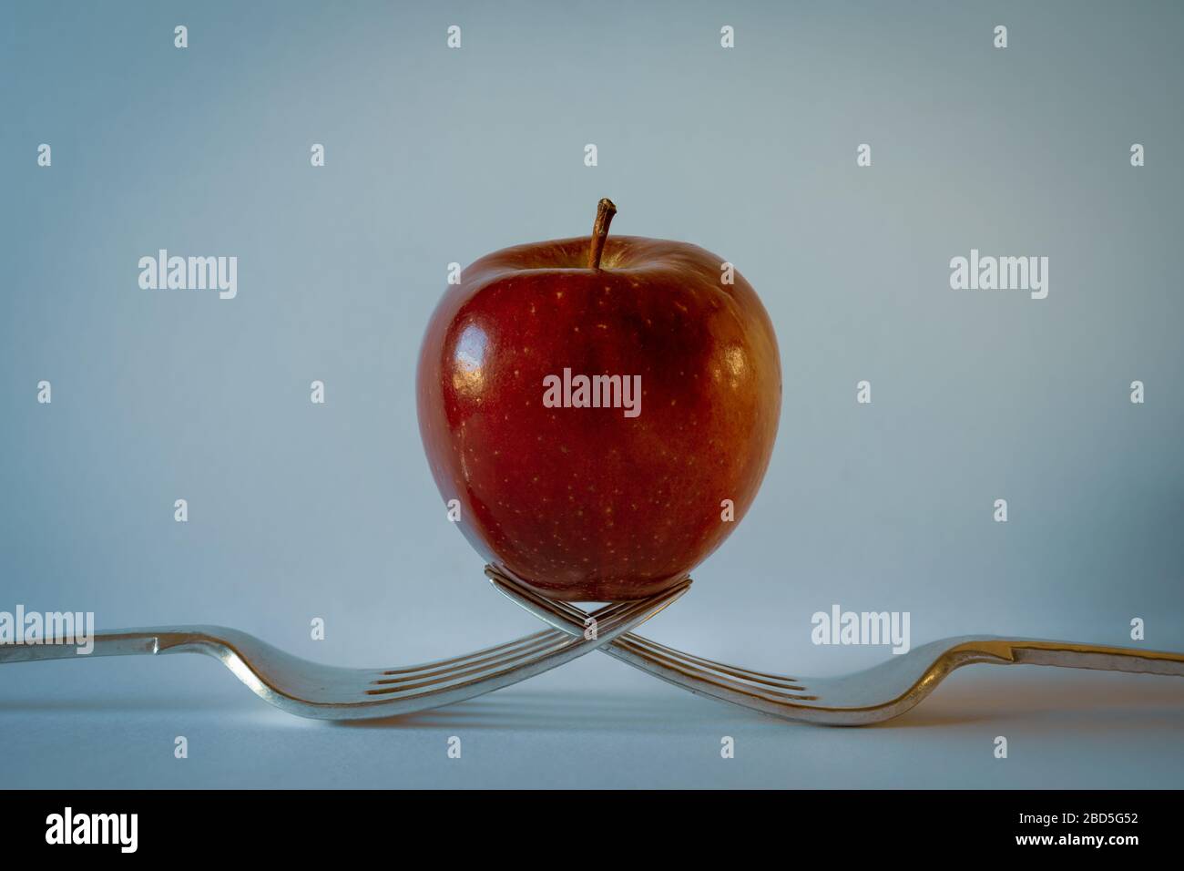 Red apple on two forks with light blue background Stock Photo - Alamy