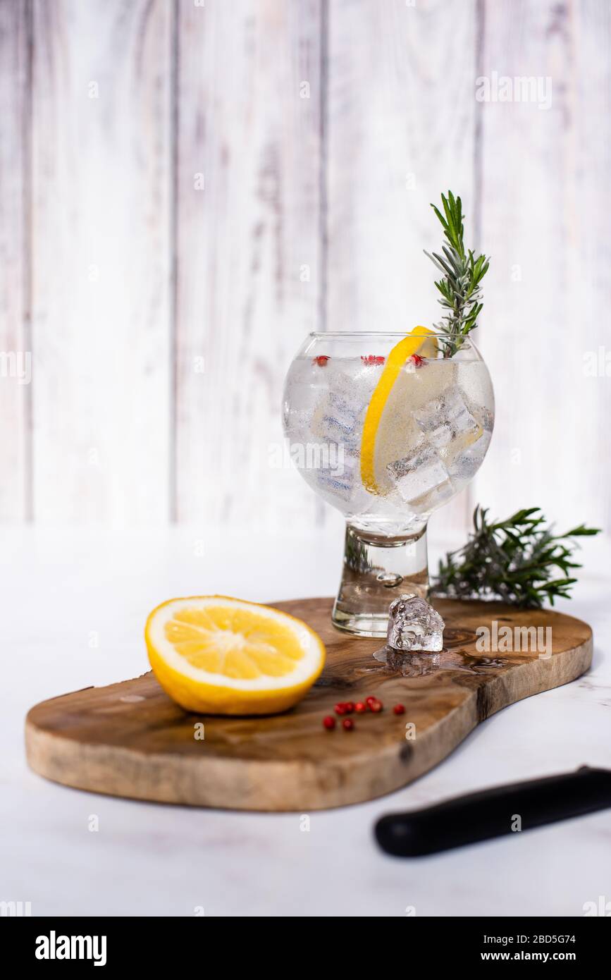 Cold Gin & Tonic cocktail with lemon garnish on wooden chopping board ...