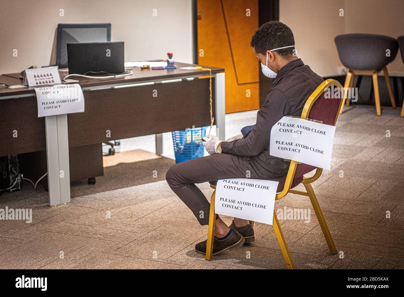 Isolated masked worker waits in an office with social distance warnings ...