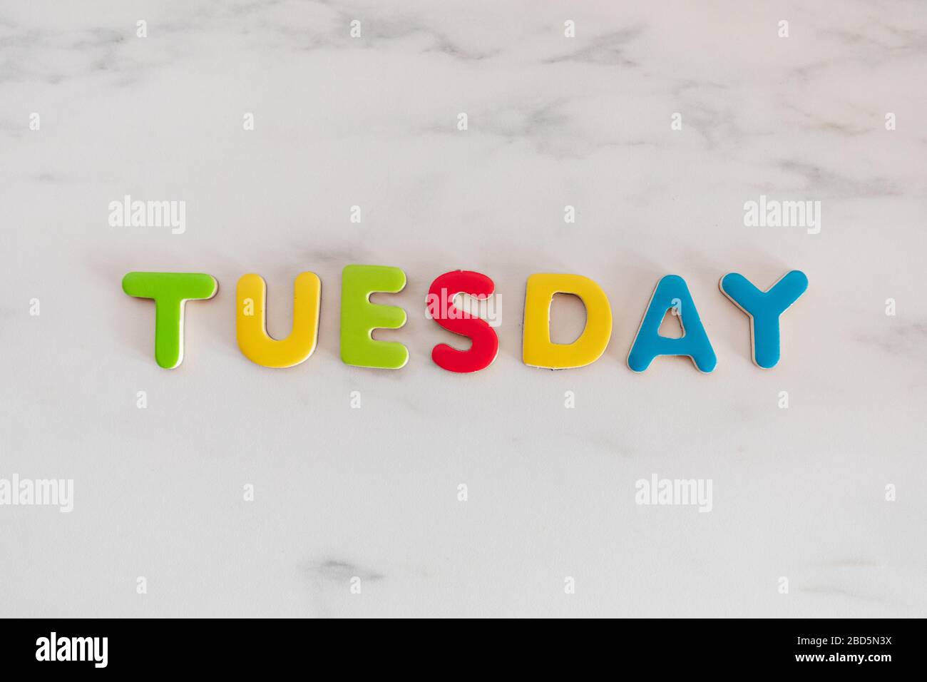 Tuesday word written with colorful letters on white marble stone ...