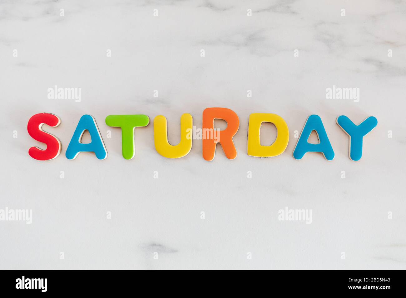 Saturday word written with colorful letters on white marble stone ...