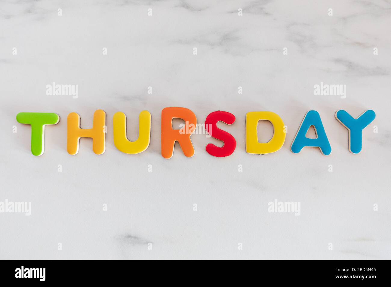 Thursday word written with colorful letters on white marble stone ...