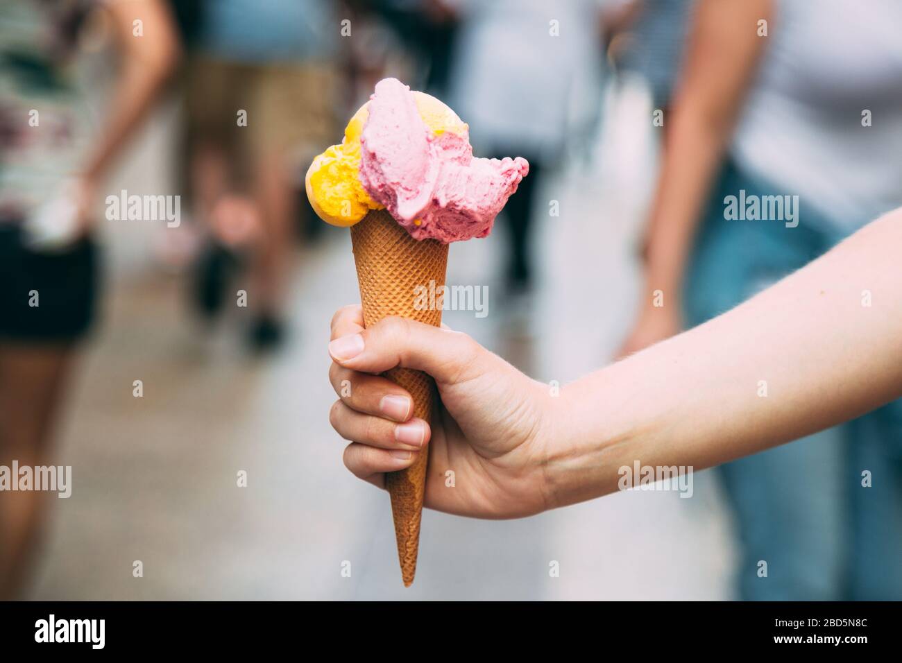 Woman hand holding an ice cream in the street full of unrecognizable ...