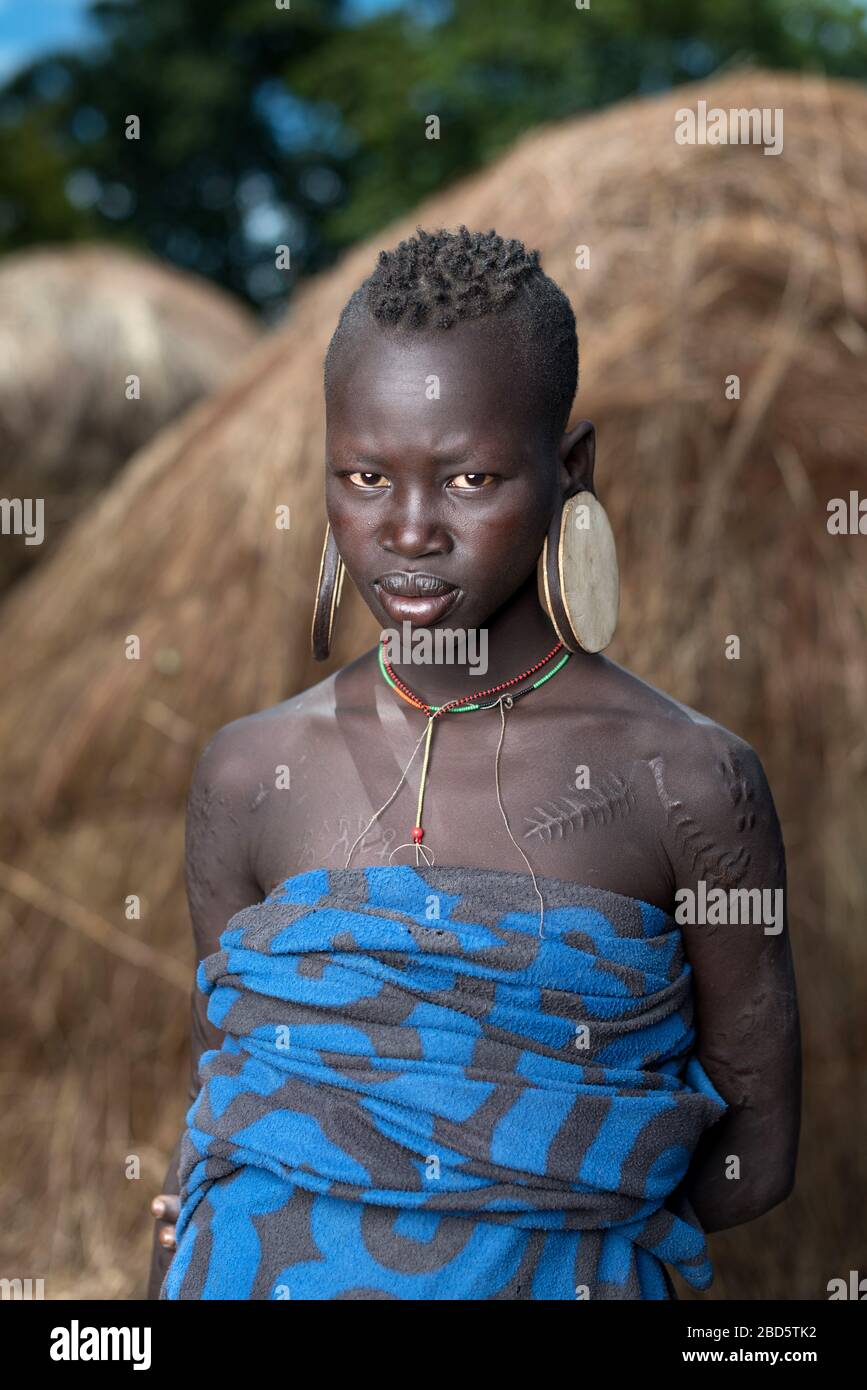 With animal skin disks inserted into distended ear lobes, a young woman ...