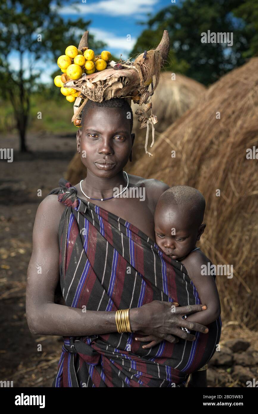 A nursing mother adorns herself with dried fruit and cattle horn, Mursi ...