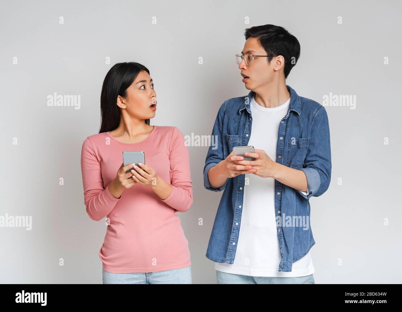 Surprised asian couple with mobile phones looking at each other Stock ...