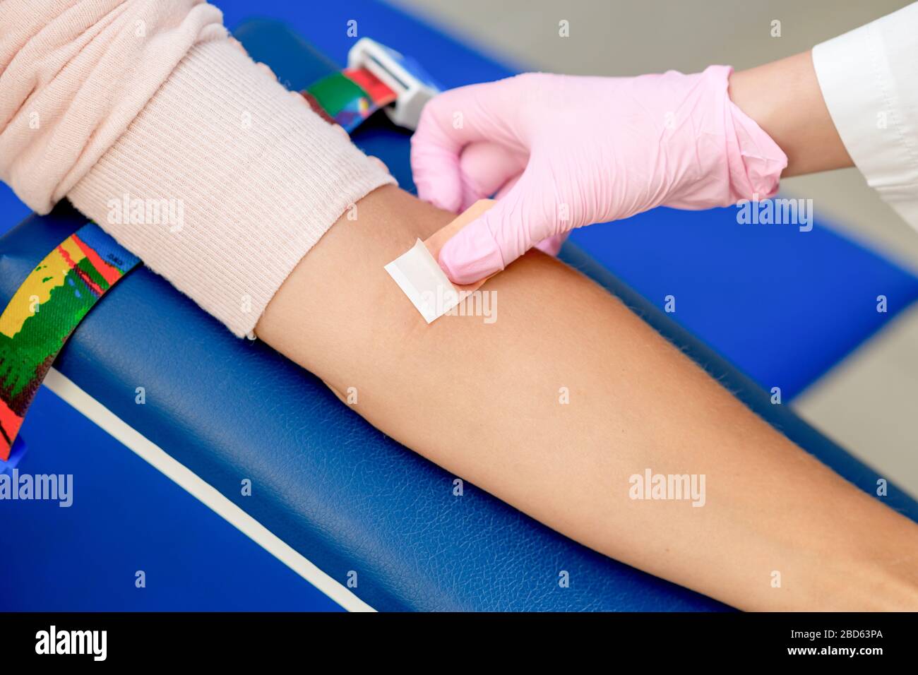 Doctor in rubber protective gloves glues an adhesive plaster on arm ...