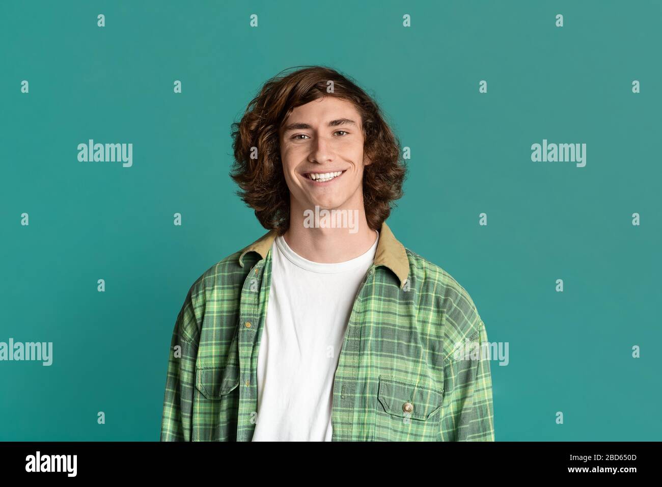Cool millennial guy with curly hair smiling on turquoise backgrund ...