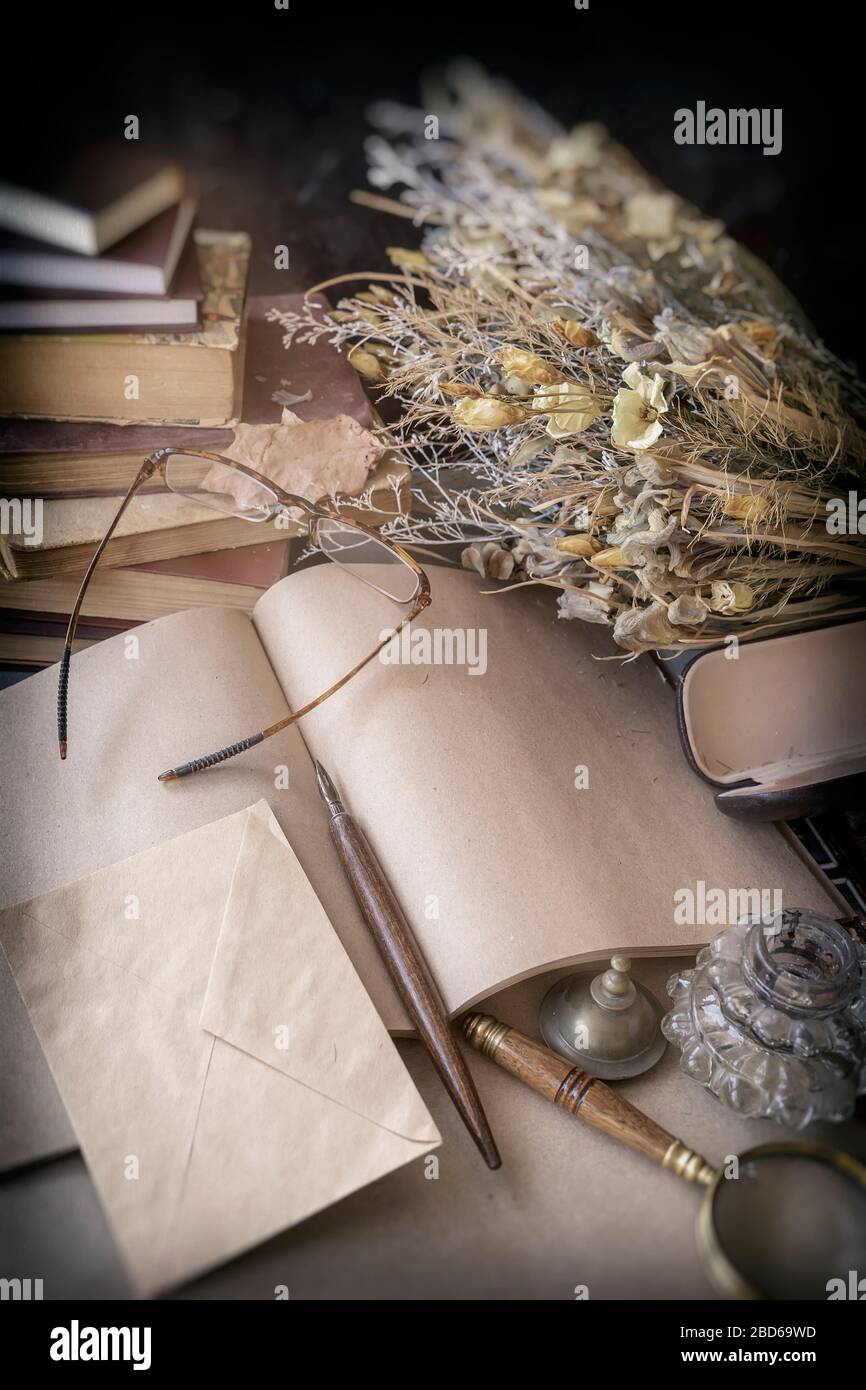 Open unwritten letter and envelope, glasses, books and a dried bouquet ...