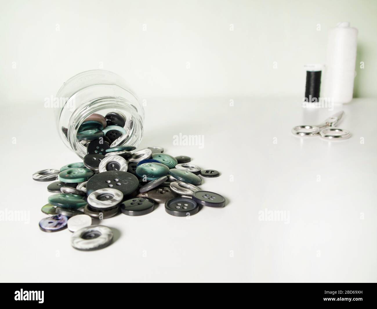 Glass jar full of clothing green, gray and black buttons, thread and ...