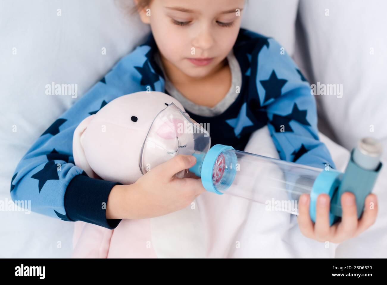selective focus of sick kid holding inhaler with spacer near bunny toy ...