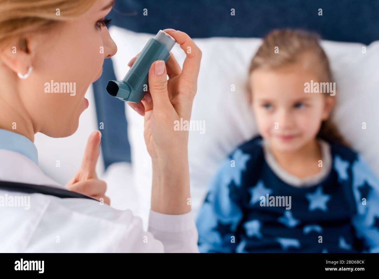 selective focus of attractive doctor with opened mouth holding inhaler ...