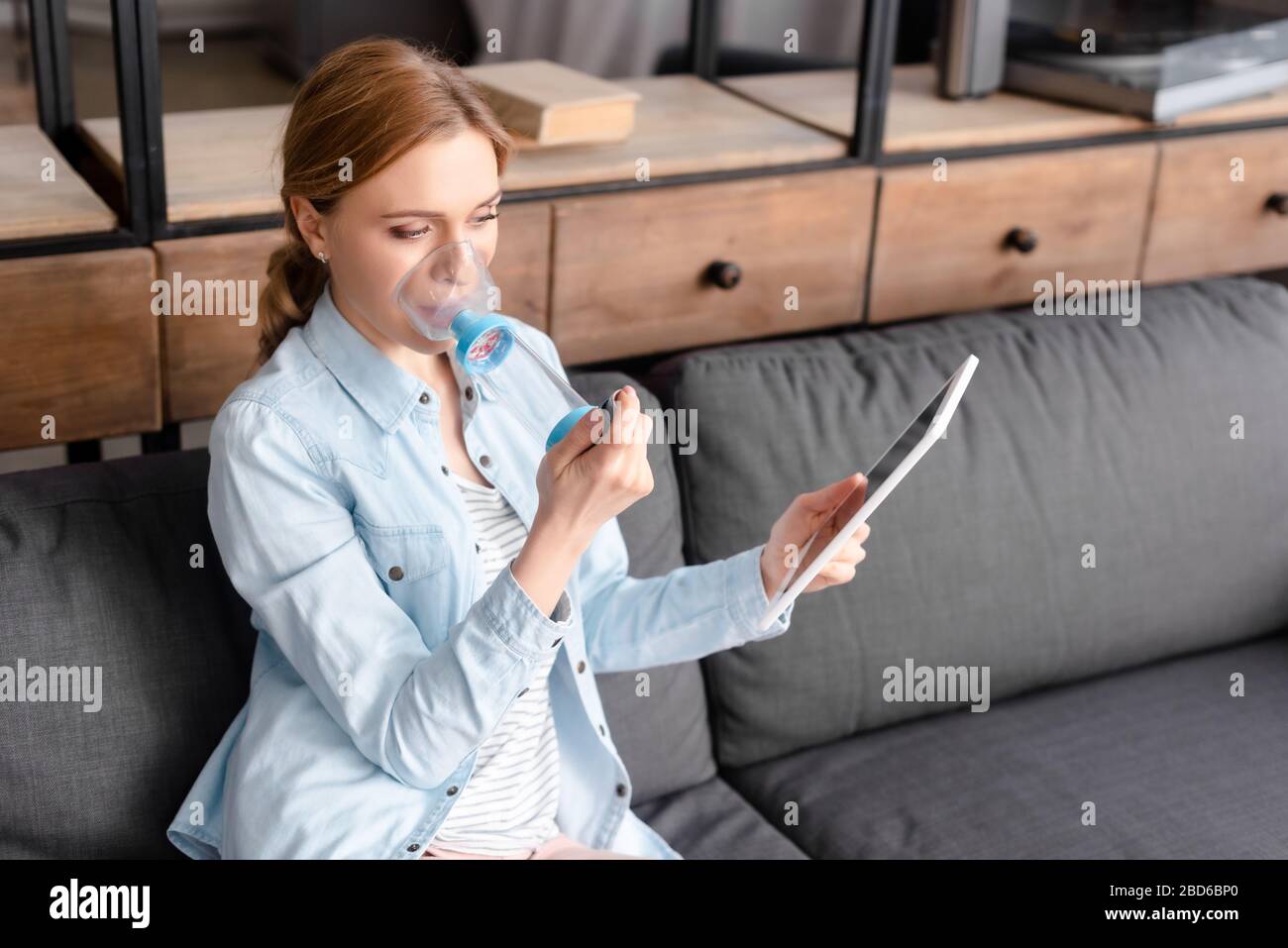 asthmatic woman using inhaler with spacer and holding digital tablet ...