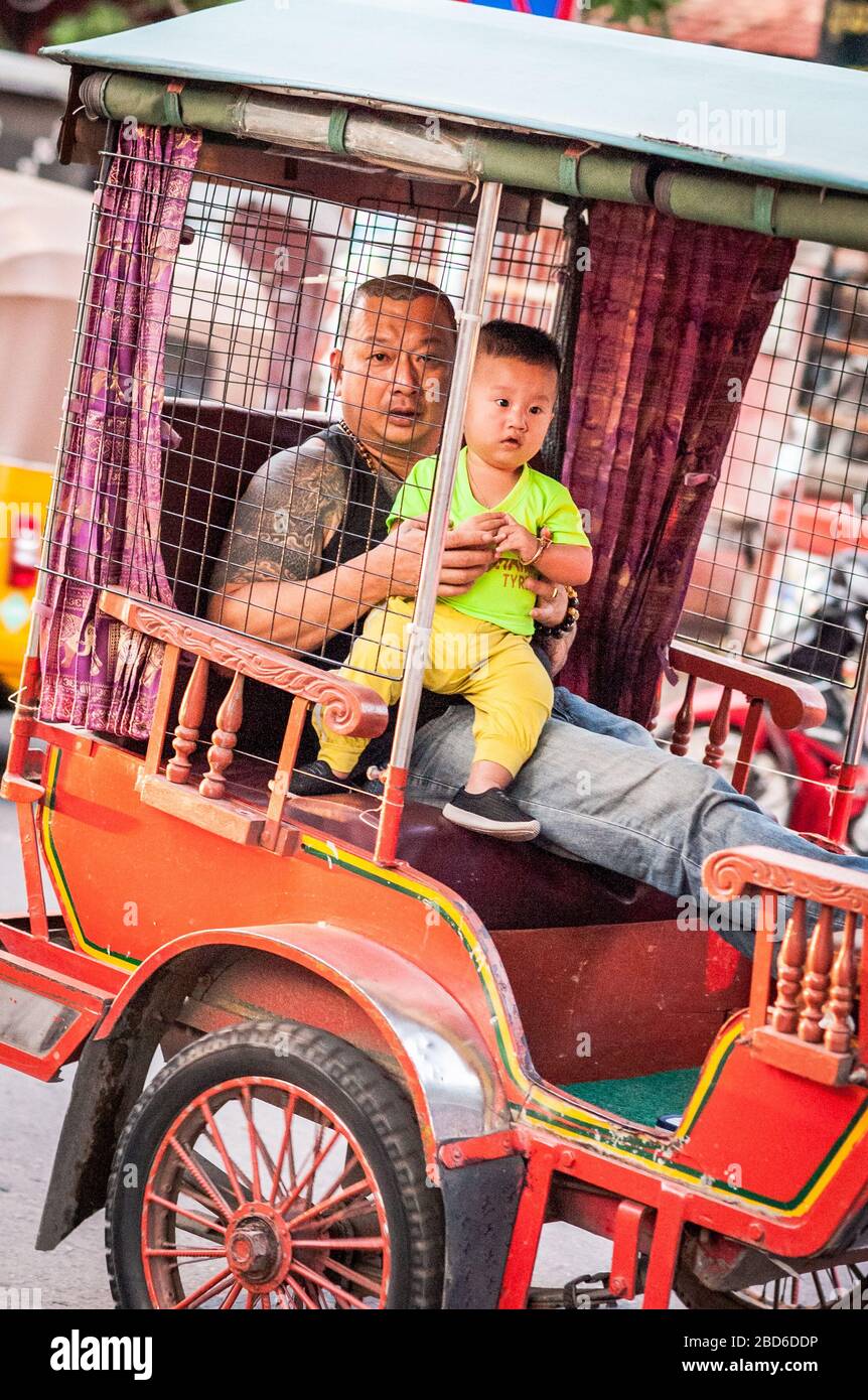 A father holds onto his baby as they sit in the back of a traditional ...