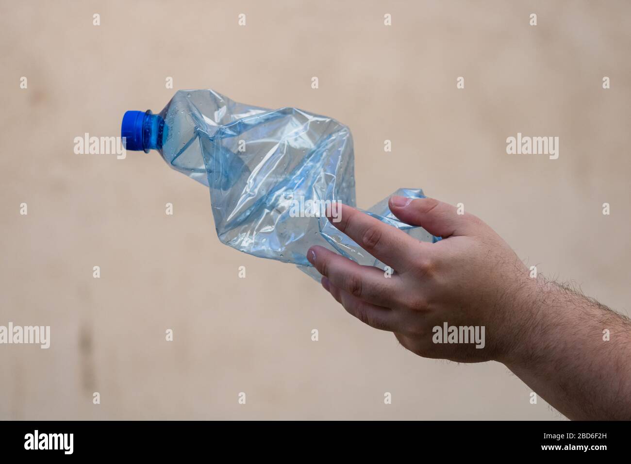 Hand holding smashed empty plastic bottle isolated on a blurred ...