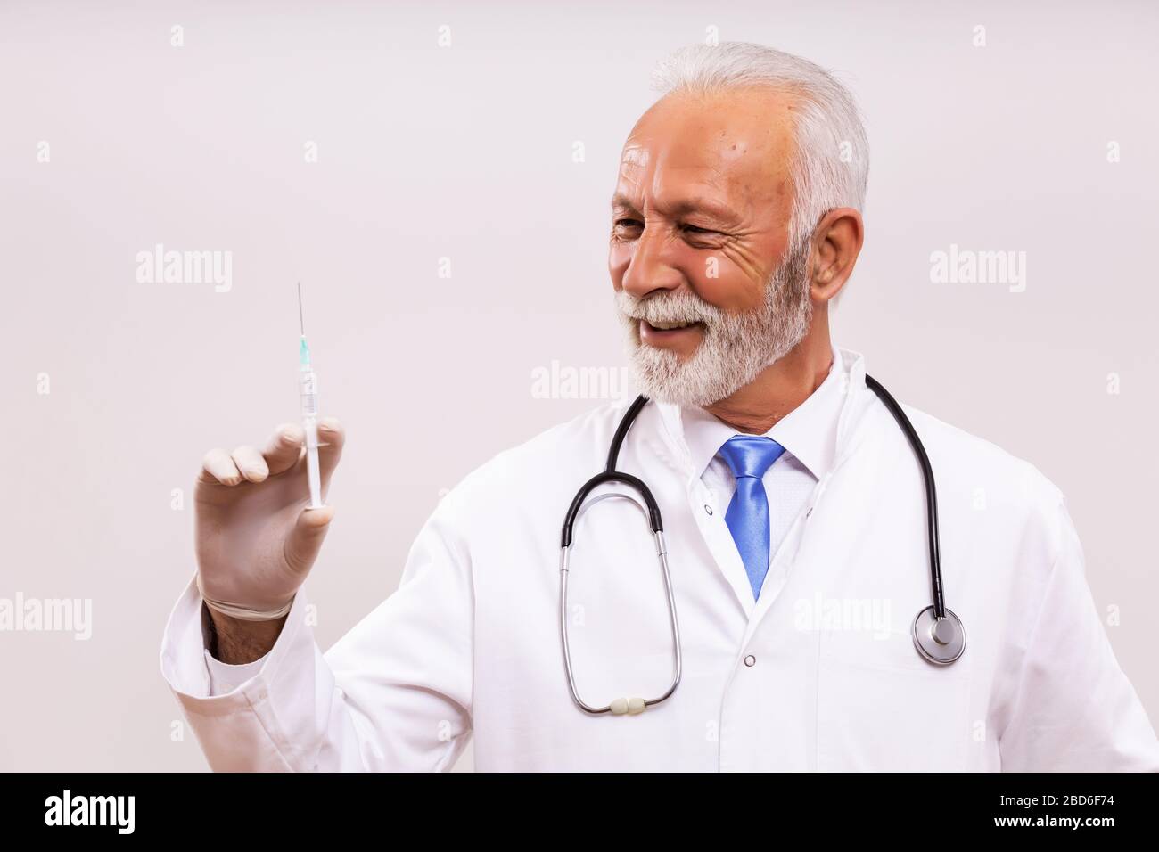 Portrait of senior doctor holding injection on gray background Stock ...