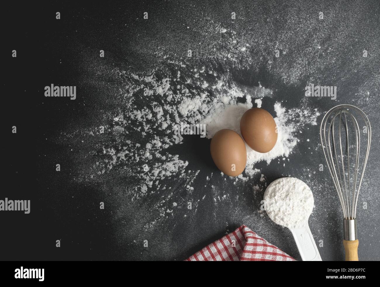 The eggs with a cup of flour and whisk on the black table spread of ...