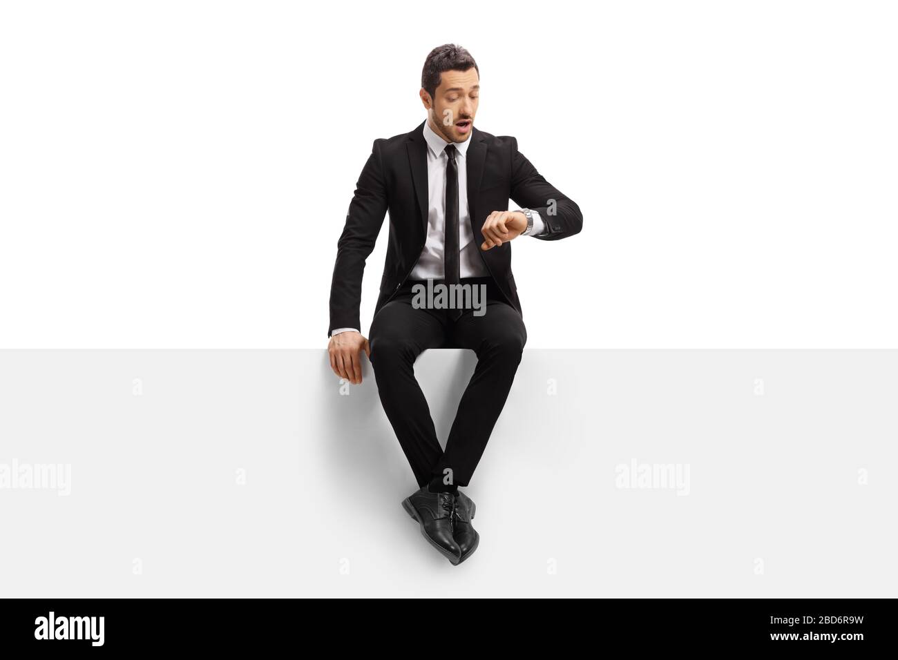 Full length portrait of a young man in a suit sitting on a panel and ...