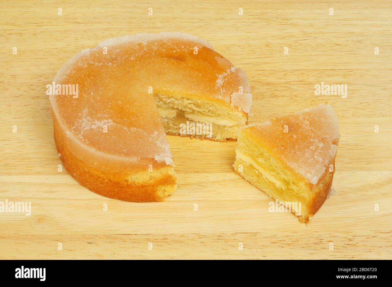 Lemon drizzle sponge cake with a slice cut out on a wooden chopping ...