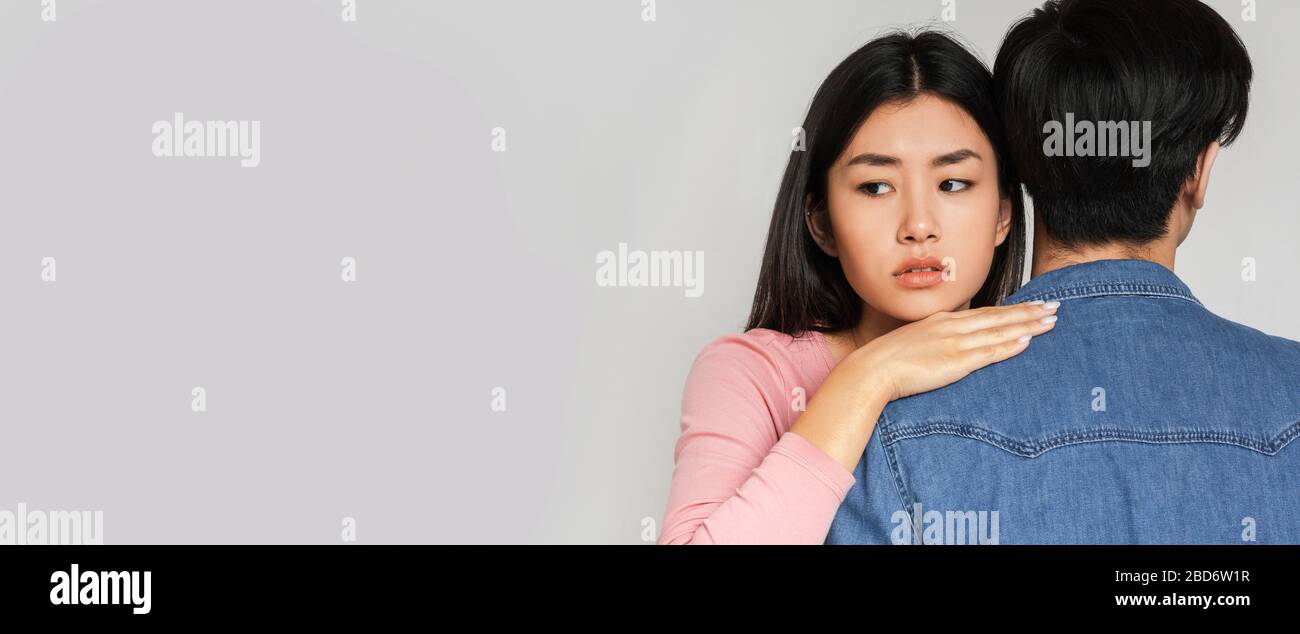 Scared asian girl hugging her boyfriend over grey background Stock ...