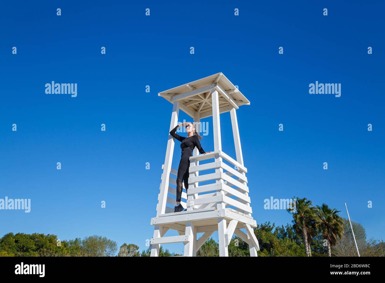 Beautiful female lifeguard stands on a tower and looks towards the sea ...