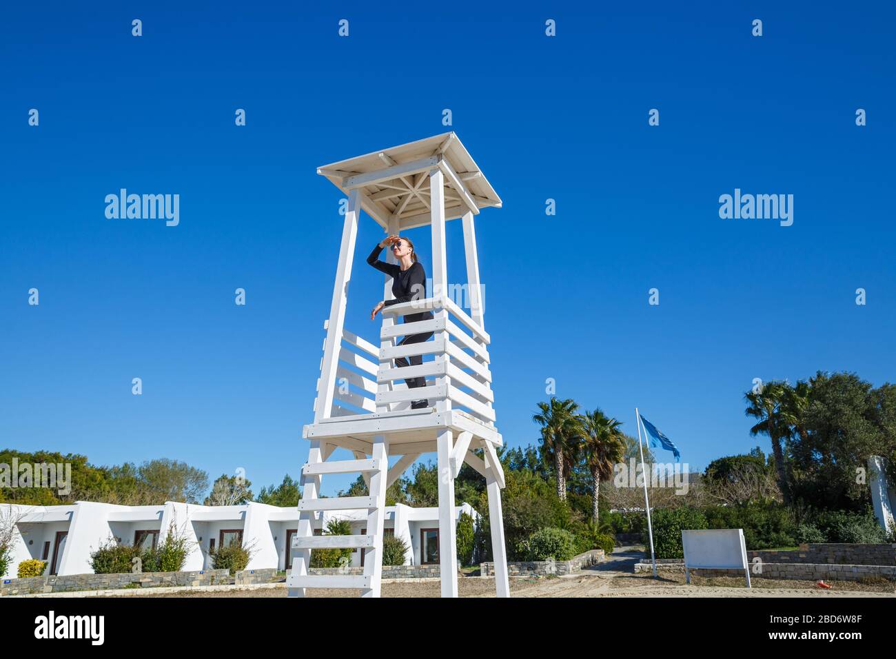 Beautiful female lifeguard stands on a tower and looks towards the sea ...
