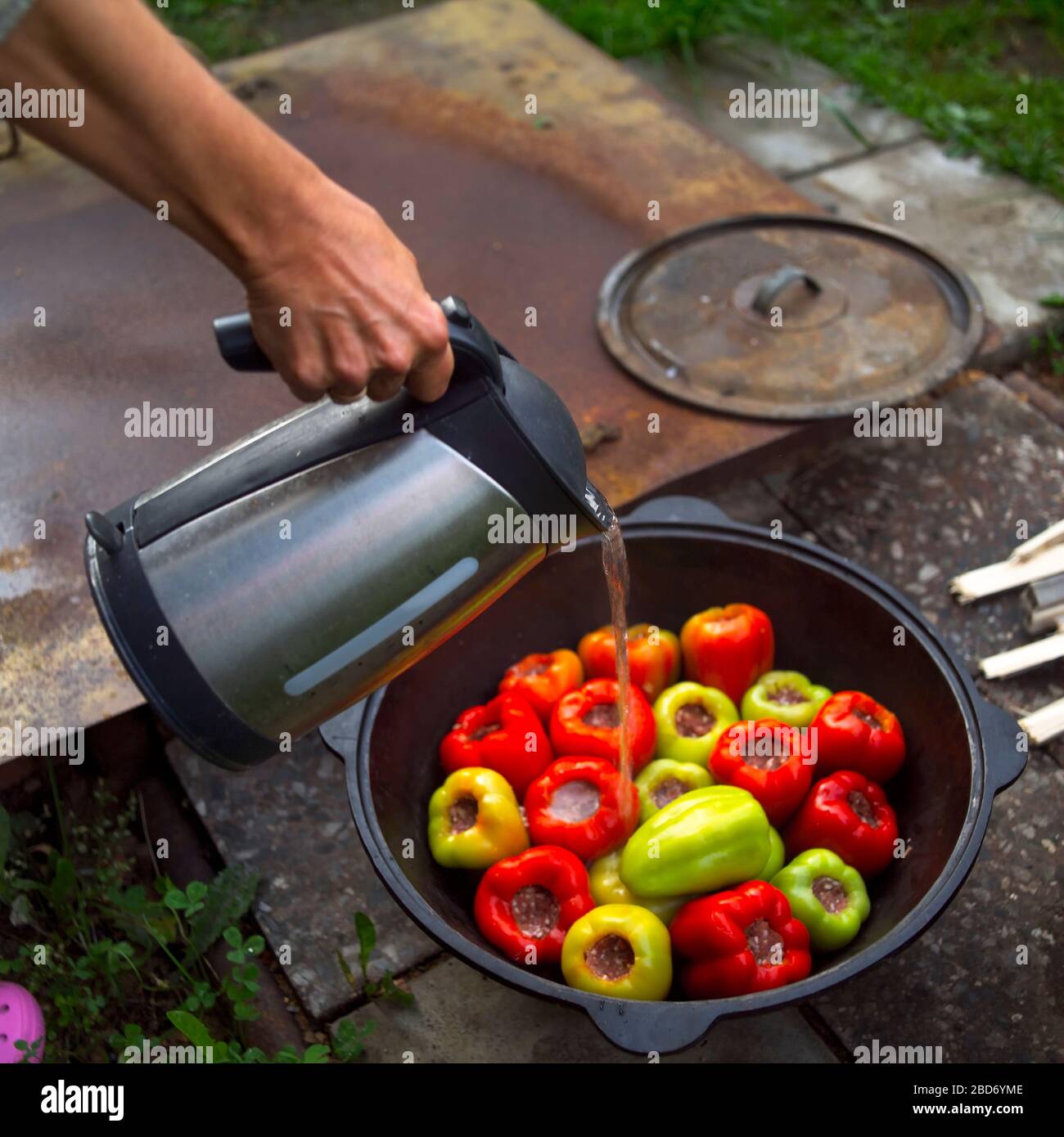 Female hand pouring hot water into a pan with cooking vegetables with ...