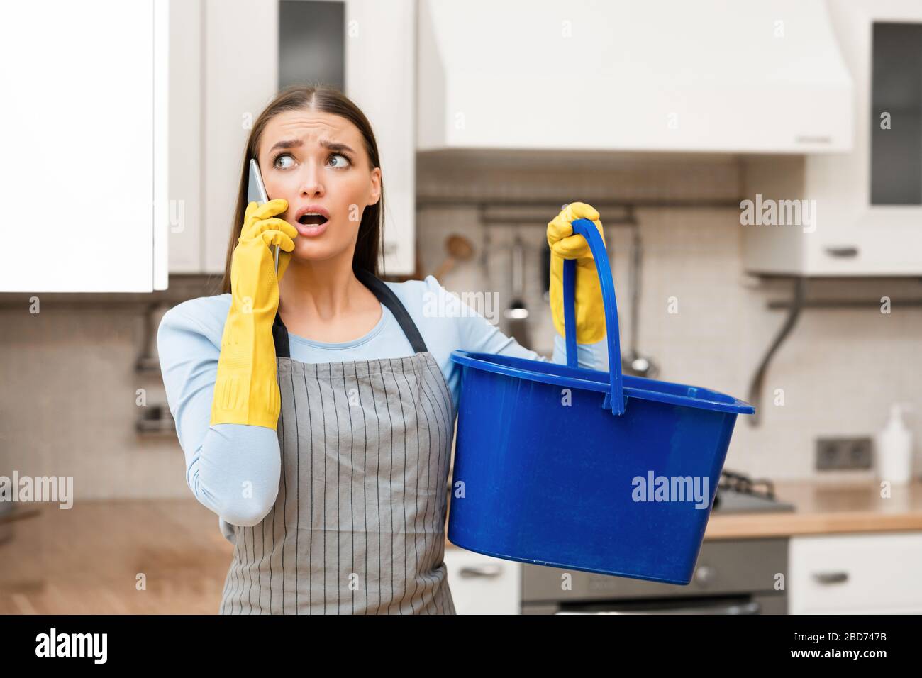 Scared young woman calling plumber holding bucket Stock Photo - Alamy