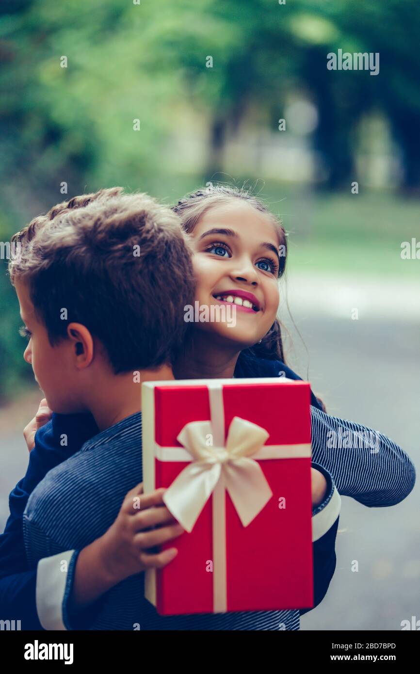Happy little child boy gives smiling girl a gift box, making a surprise ...