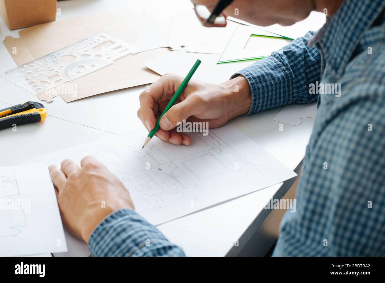 Man drawing scematics for production of boxes. Close up. From behind ...