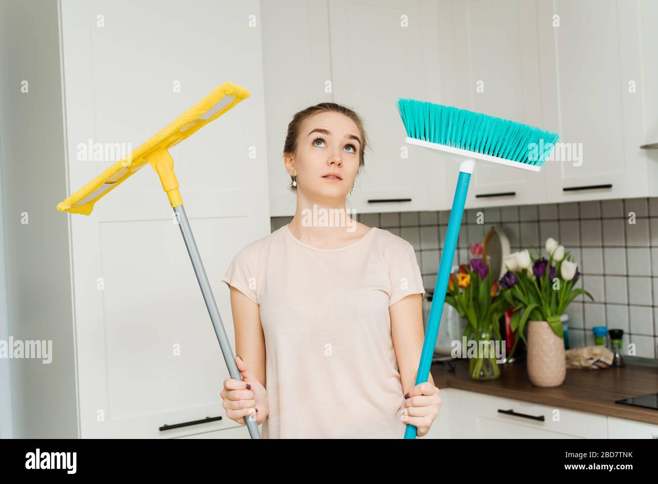 A beautiful woman holds a mop and brush for cleaning and mopping in her ...