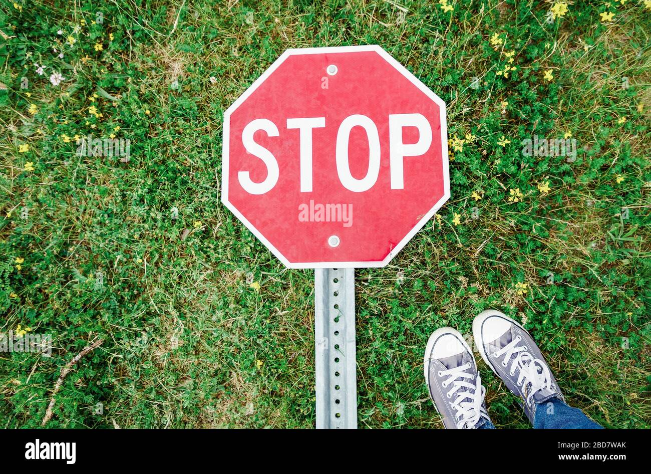 Feet and red stop sign on the green grass background. Prohibition ...
