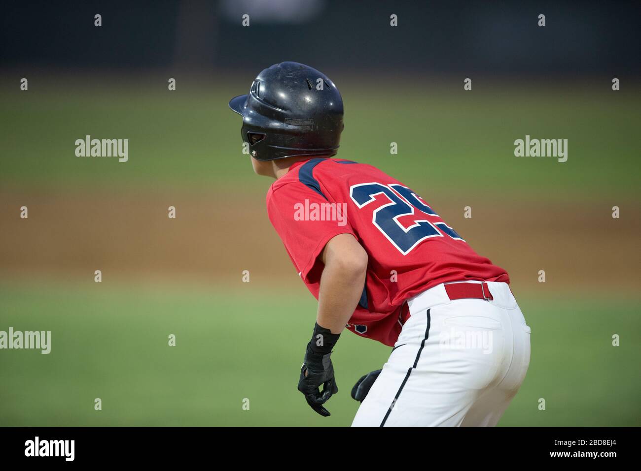 Looking over the shoulder of teen baseball runner leading off base ...