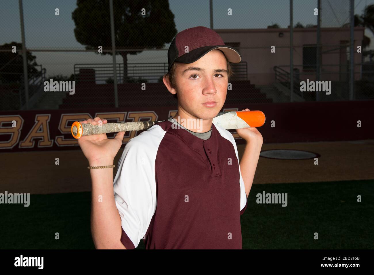 Portrait of a High School baseball player in maroon uniform holding his ...