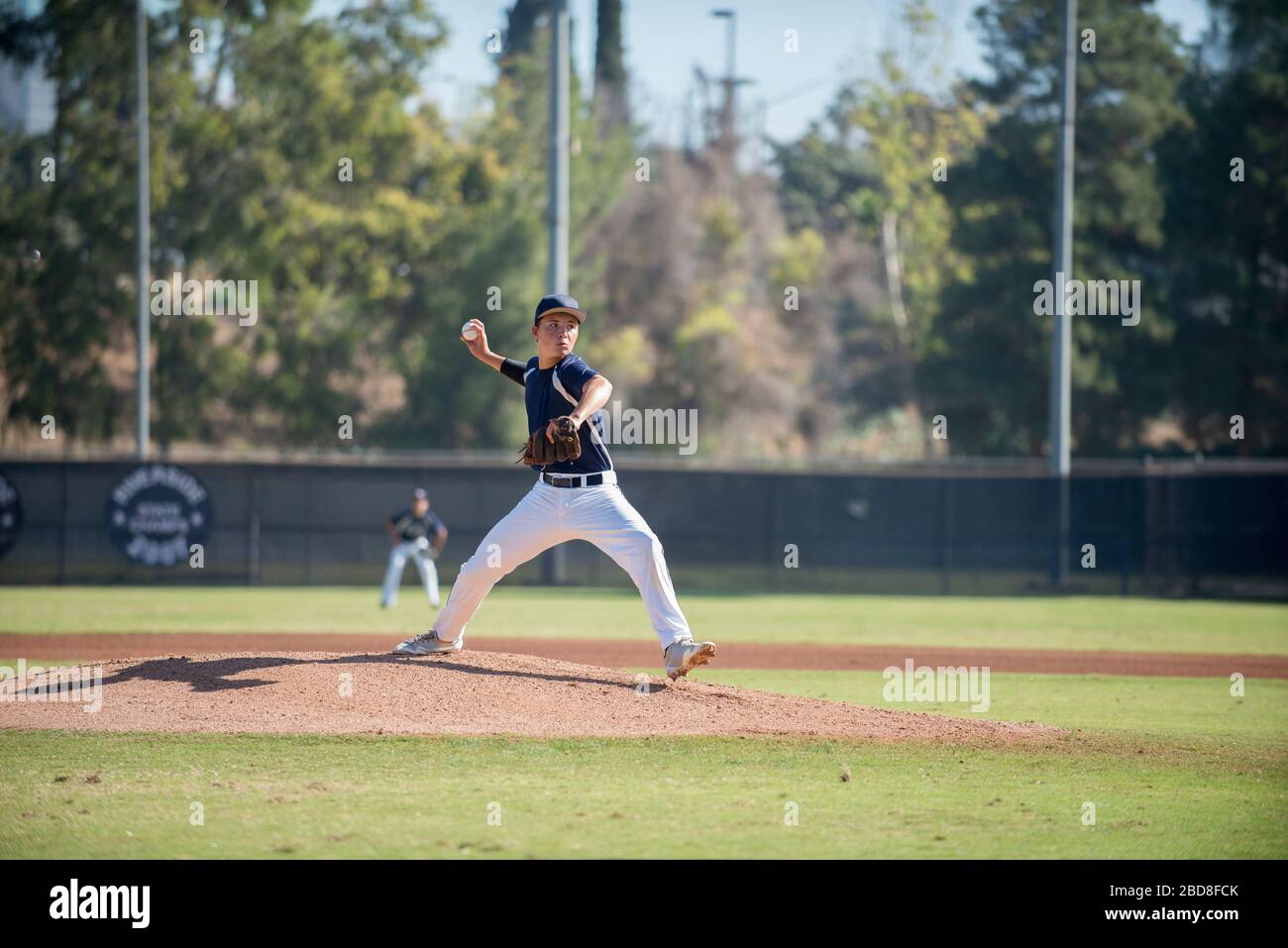 teen baseball player pitcher in blue uniform in full wind up on the ...