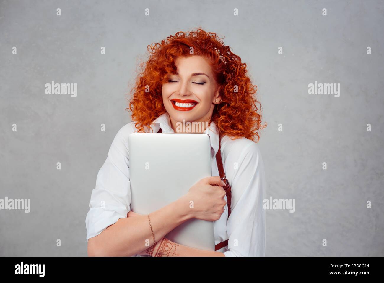 I love my laptop. Red head curly business woman in white shirt hugging ...
