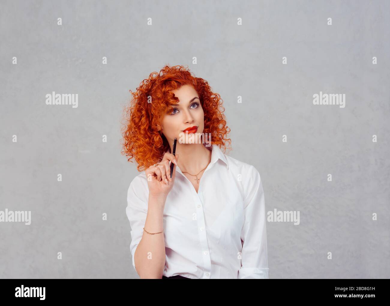 Doubtful business woman thinking pen on cheek. Red head curly ginger ...