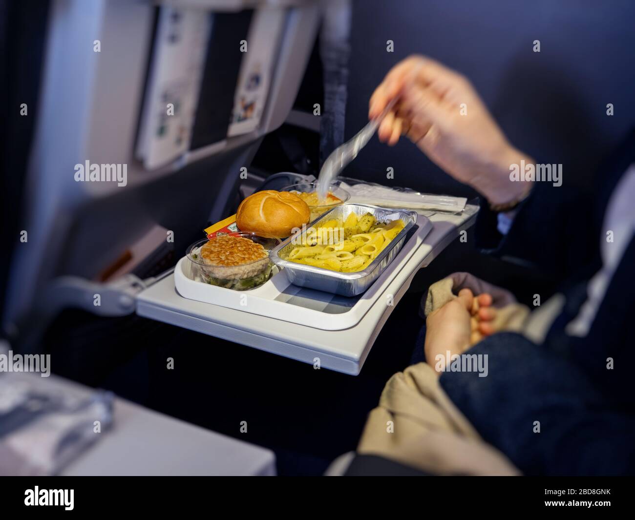 Side view of woman eating delicious meal in modern aircraft economy ...