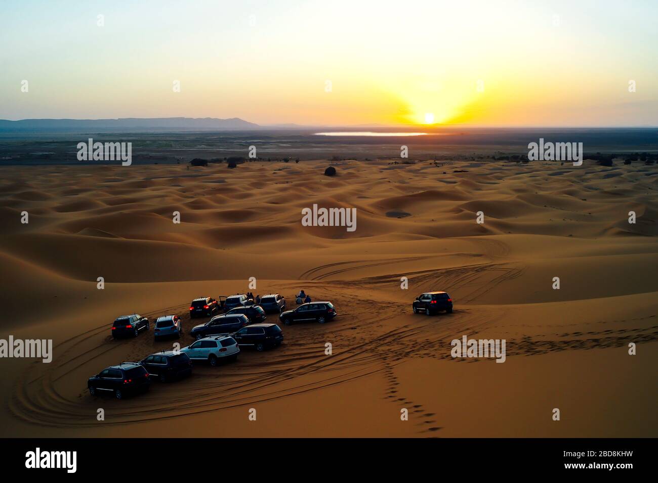 People watch the sunset in the Moroccan desert from their 4x4 cars ...