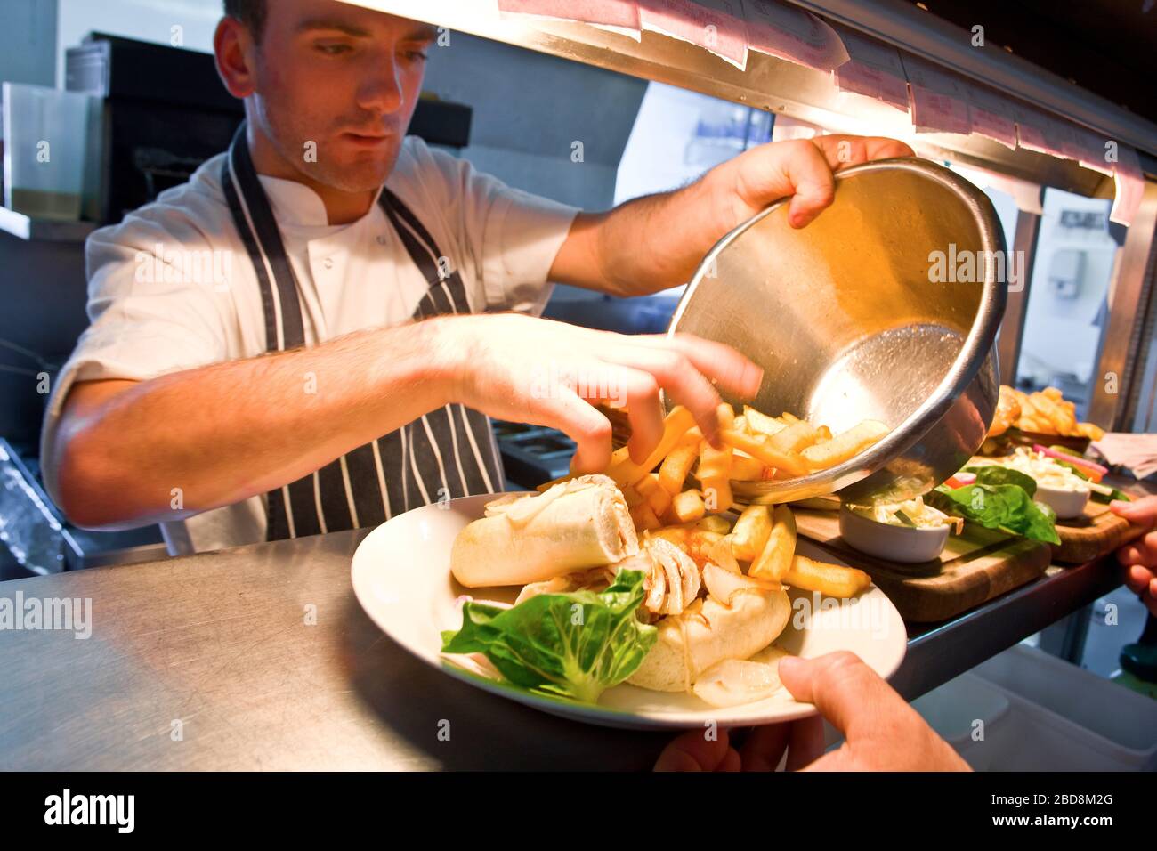 chef adds french fries to a dish at commercial kitchen Stock Photo - Alamy