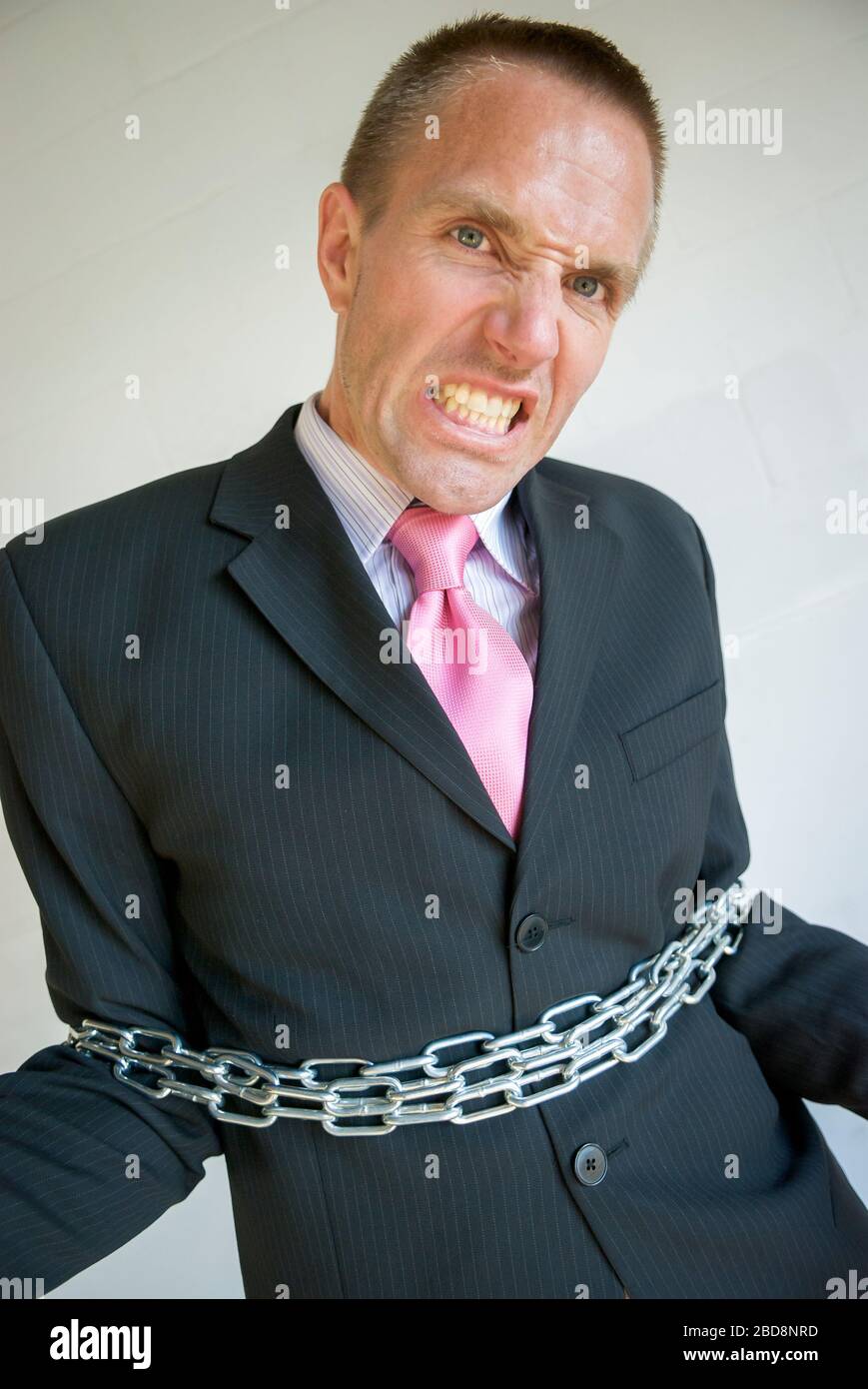 Businessman struggling against the loops of metal chain wrapped around ...
