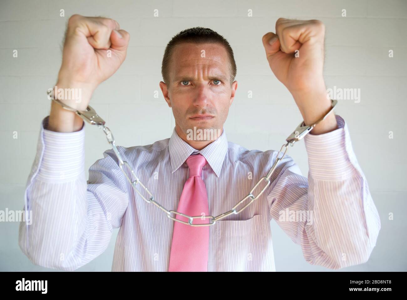 Unhappy businessman holding up handcuffed hands chained together ...