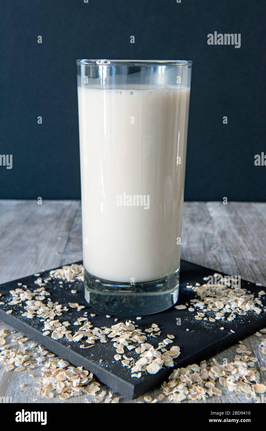 Vegan oat milk or drink in glass with oats strewn around on black tile ...